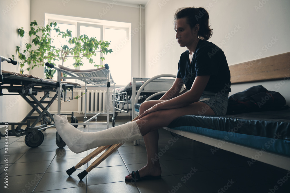 A woman with a broken leg sits on a hospital couch. Leg injury. Loss of ...