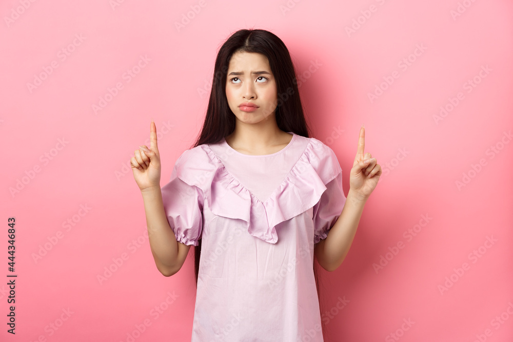 Sad pitiful asian girl sulking, pointing and looking up with ...