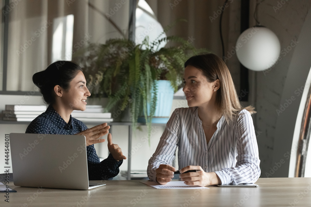 Diverse female office employees discussing project, talking at meeting ...