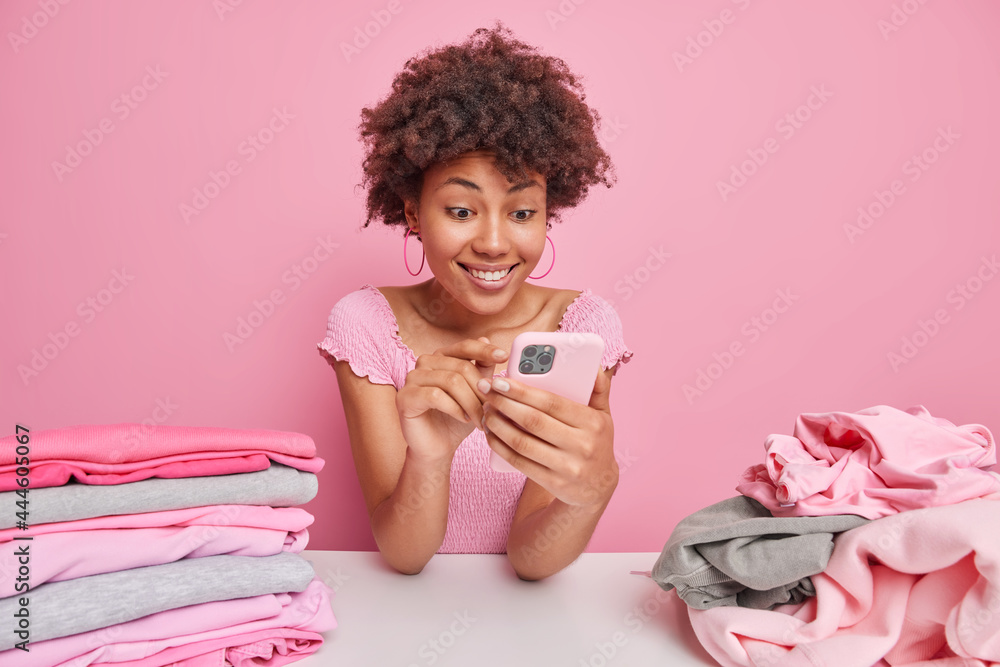 Happy dark skinned young woman with curly hair checks newsfeed on ... Happy dark skinned young woman with curly hair checks newsfeed on ...
