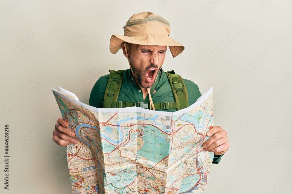 Handsome man with beard wearing explorer hat holding map angry and mad ...