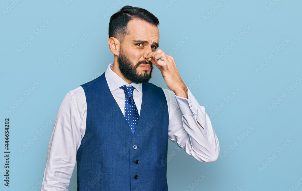 Young man with beard wearing business vest smelling something stinky ...