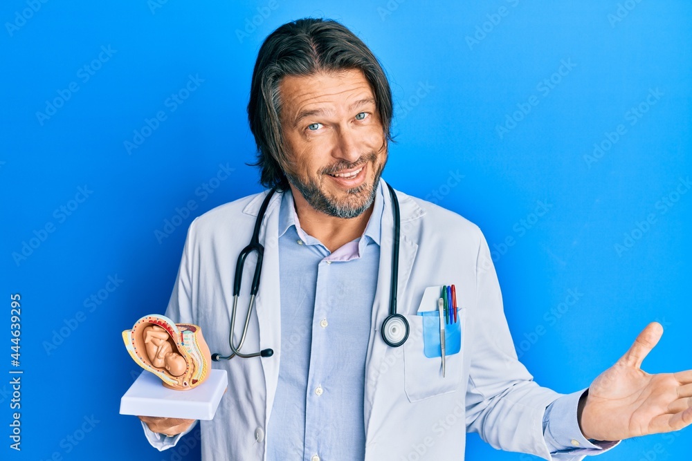 Middle age handsome gynecologist man holding anatomical model of female ...