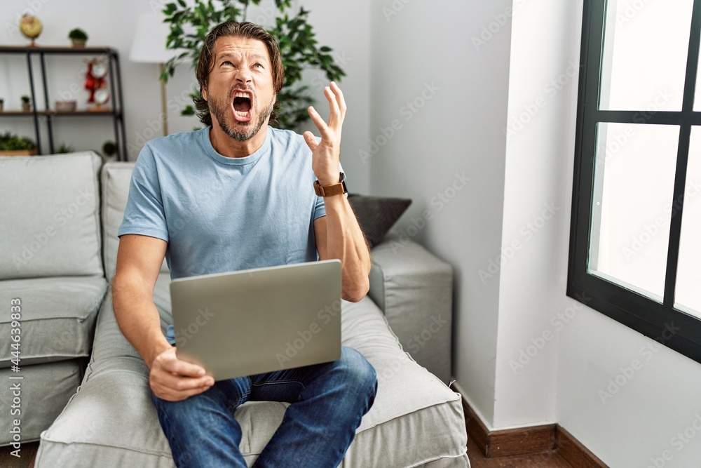 Handsome middle age man using computer laptop on the sofa crazy and mad ...