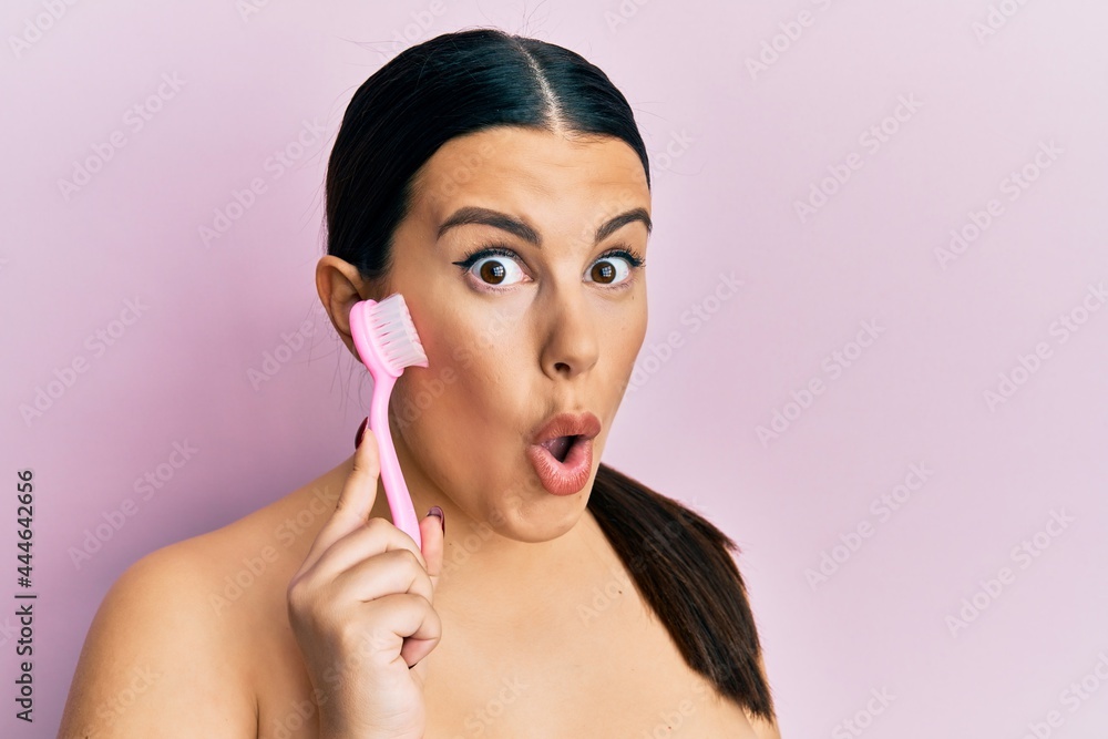 Beautiful brunette woman using facial exfoliating brush scared and ...