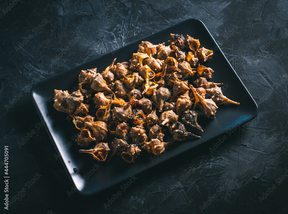 Mollusks called “Cañaillas” cooked in a black rectangular plate on a ...