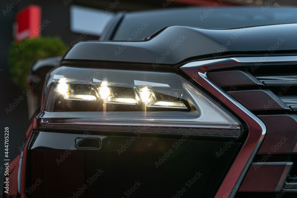 Front illuminated headlights of a black luxury modern car. Close up ...