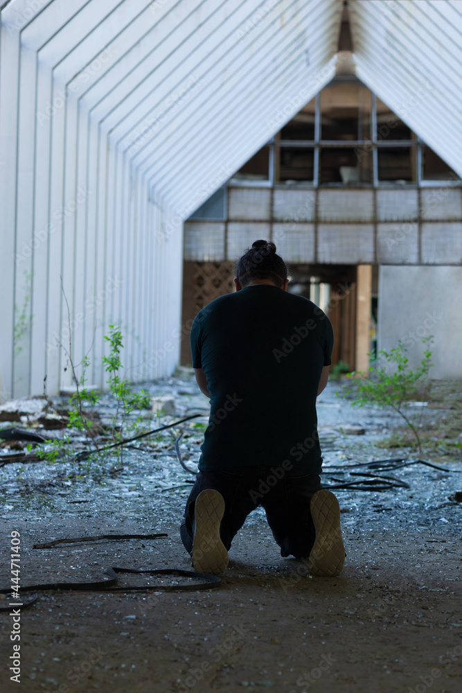 Man in dark clothes kneeling in despair in destroyed church building ...