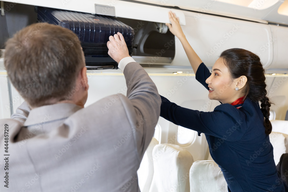 flight attendant helping passenger with carry on luggage to overhead ...