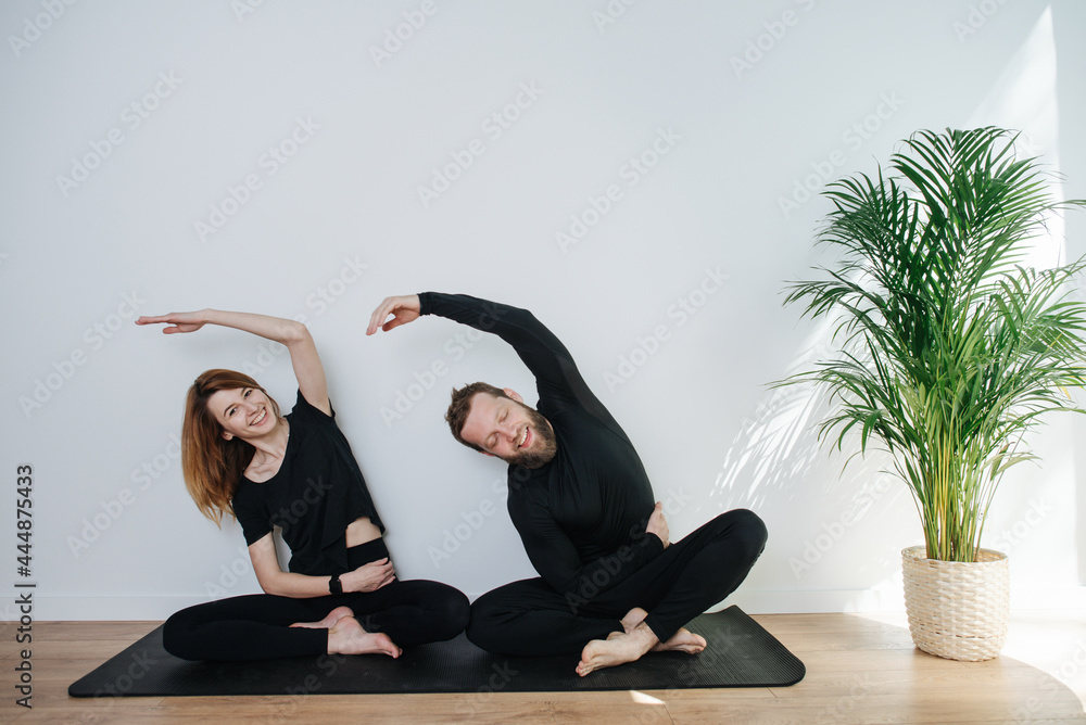 Joyous couple stretching next to each other, sitting on a single mat ...