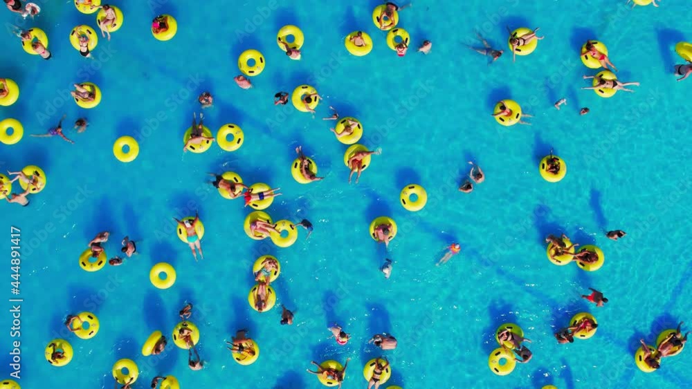 Public pool, water park, people in the pool on yellow swimming rings ...