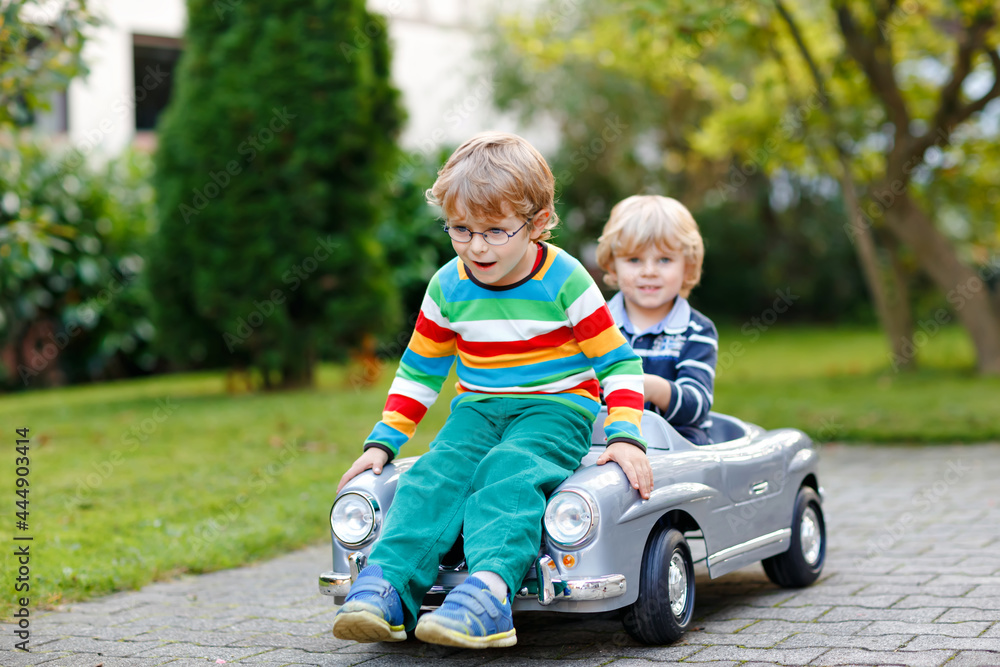 Two little preschool boys playing with big old toy car in summer garden ...