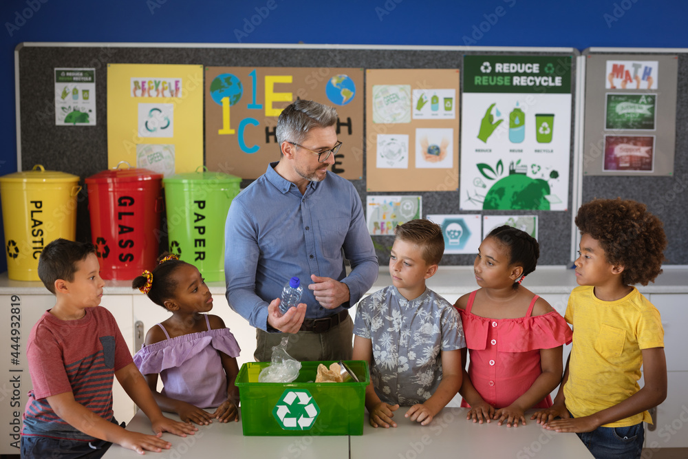 Caucasian male teacher teaching group of diverse students to recycle ...