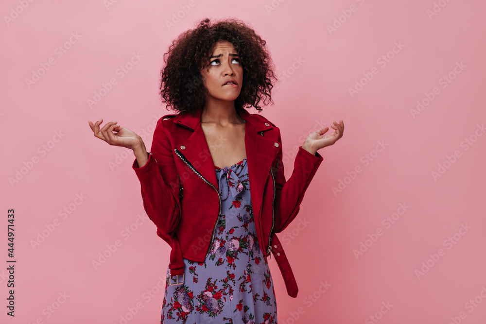 Curly woman in red jacket and dress with incomprehension posing on pink ...