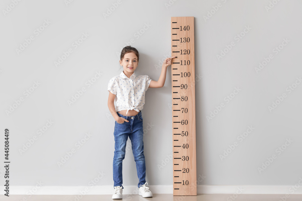 Little girl measuring height near light wall Stock Photo | Adobe Stock