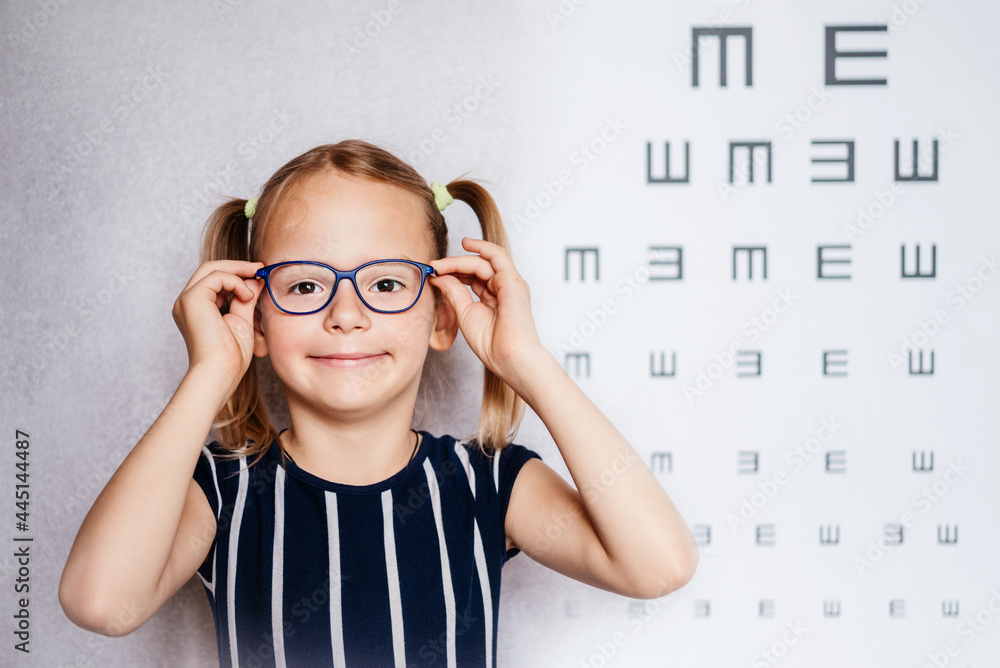 Happy little girl wearing eyeglasses taking eyesight test before school ...