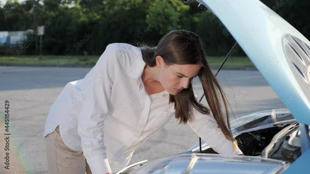 Young upset woman driver standing near the broken car with open hood ...