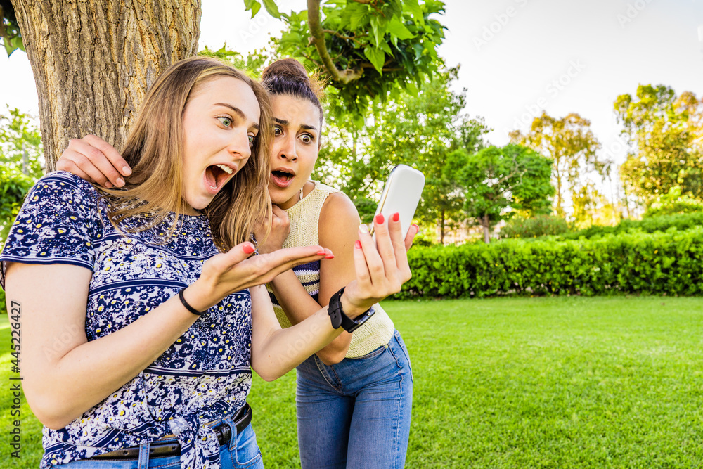 Two girls best friends look amazed at smartphone with disbelief ...