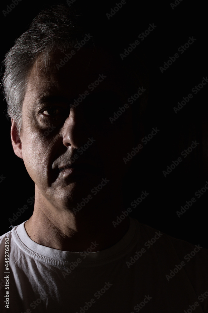 color portrait of shaved man in low key with half face in harsh shadows ...
