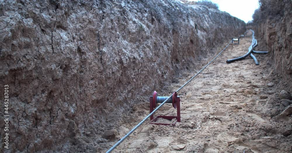 Deep trench with coils dragging steel cable across the ground ...