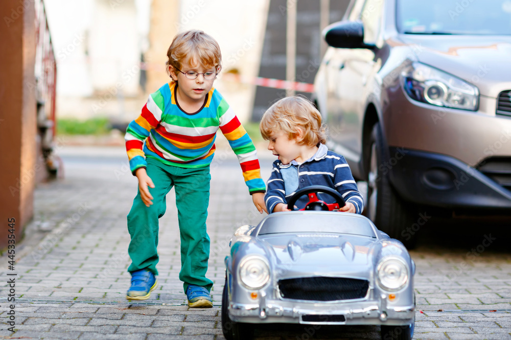 Two little preschool boys playing with big old toy car in summer garden ...