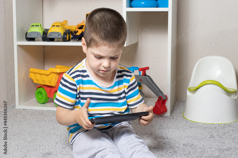 A little boy 3-4 years old looks into the screen of the tablet ...