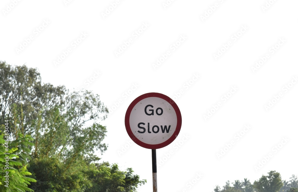 Round "go slow" road sign surrounded by trees under a cloudy sky Stock ...
