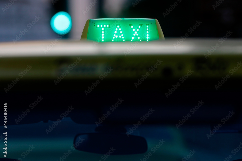 Taxi cab sign illuminated on top of vehicle at nighttime. City traffic ...