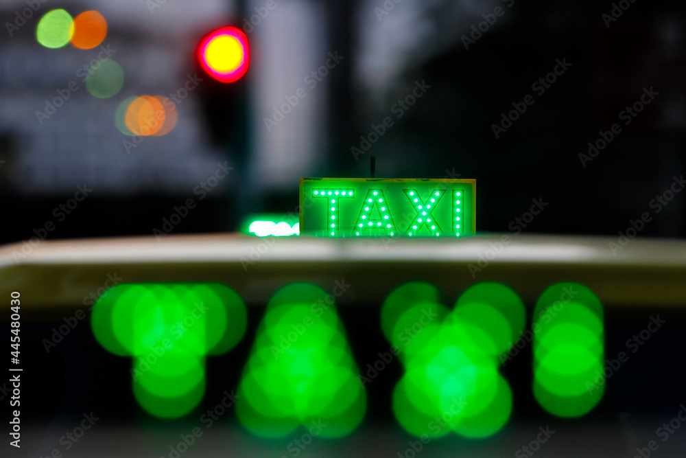 Taxi cab sign illuminated on top of vehicle at nighttime. City traffic ...