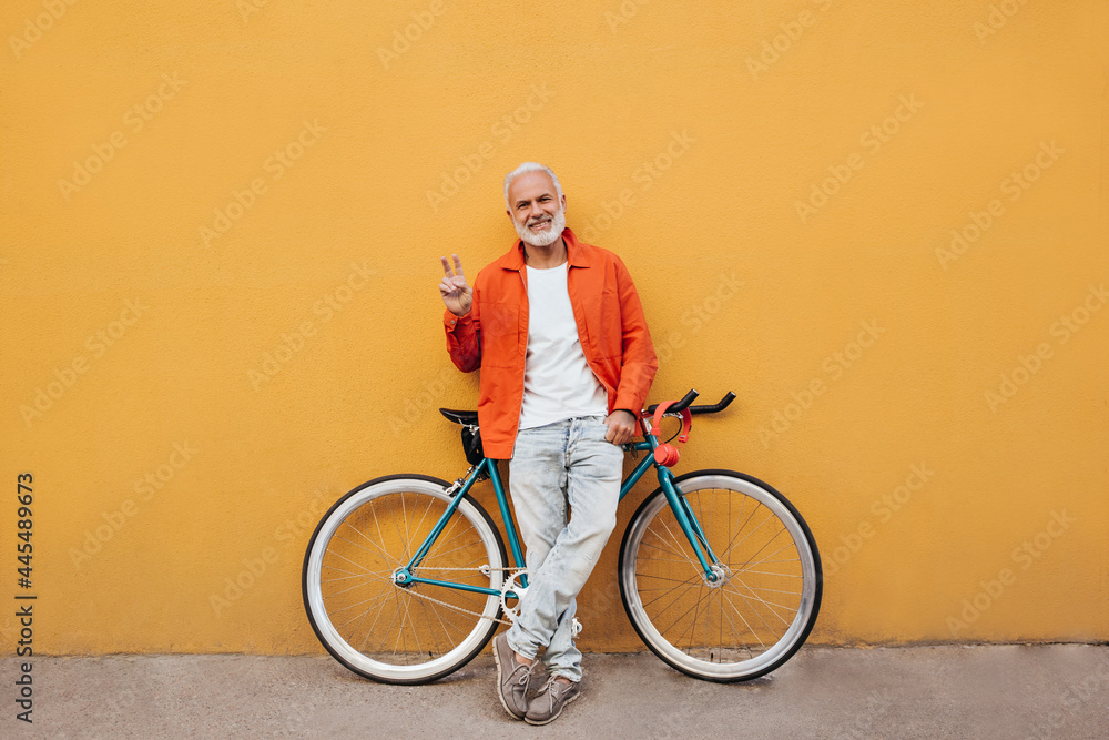 Full length shot of man showing peace sign and posing with bicycle ...