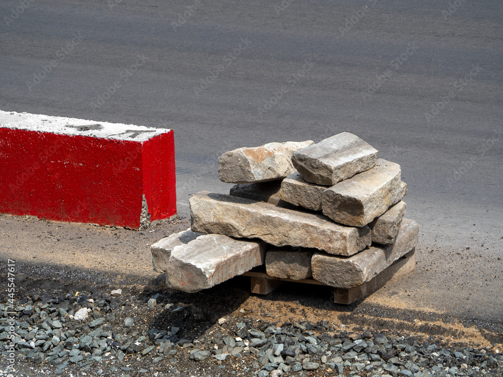 Old used curbs are stacked at the edge of an asphalt road next to a red ...