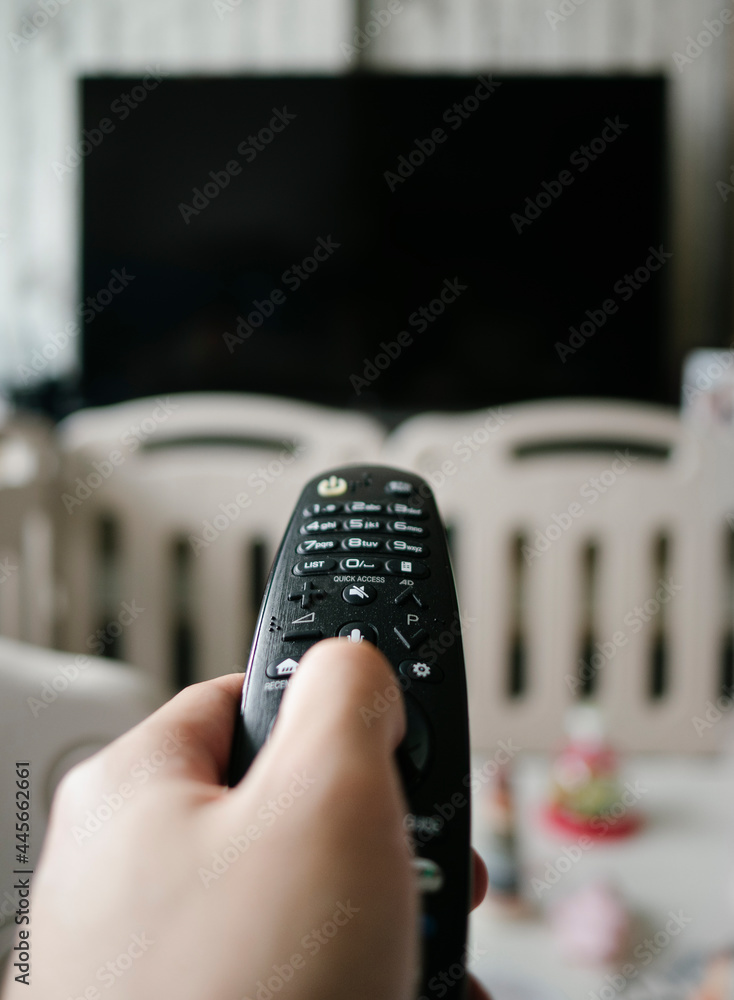 Hand holding remote control pointing at flat screen tv with child play ...