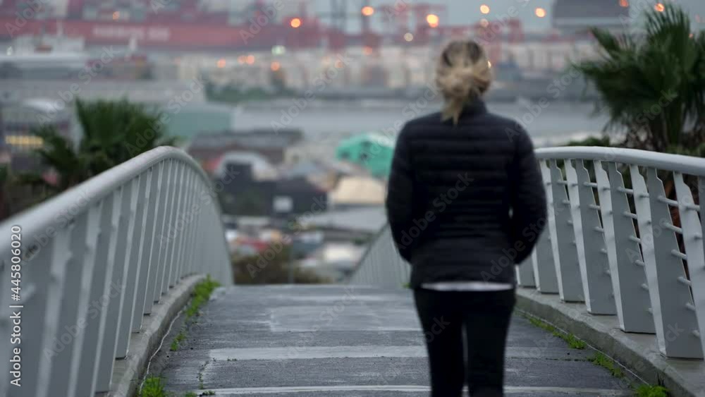 A young woman, alone and in thought, walks with hands in pockets, over ...