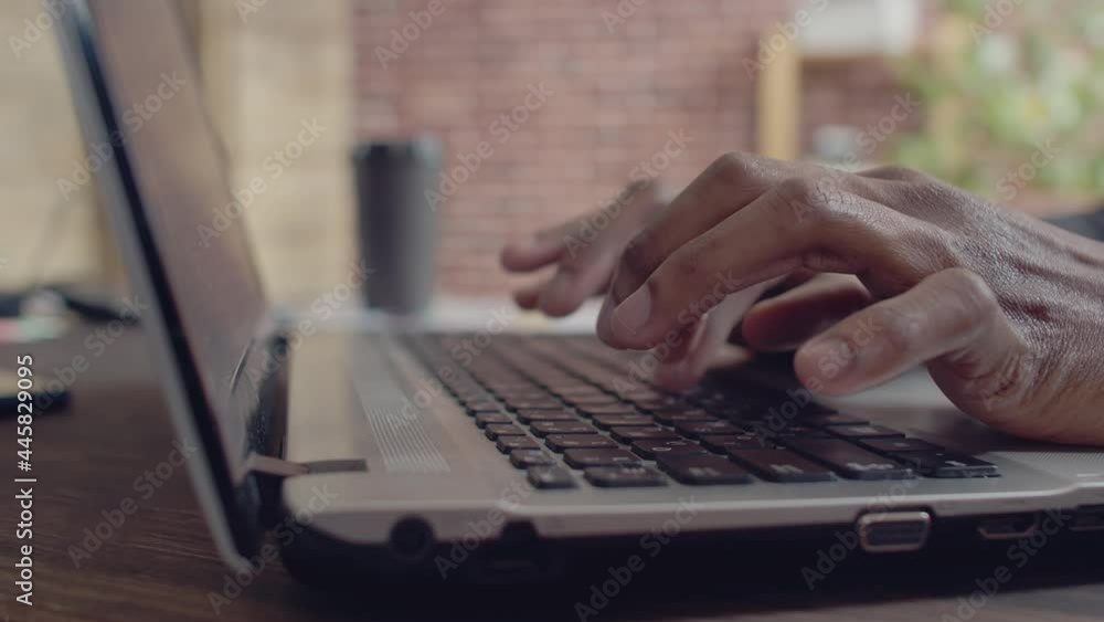 Close-up of the hands of a black man typing fingers on laptop keyboard at an office table. Black ...