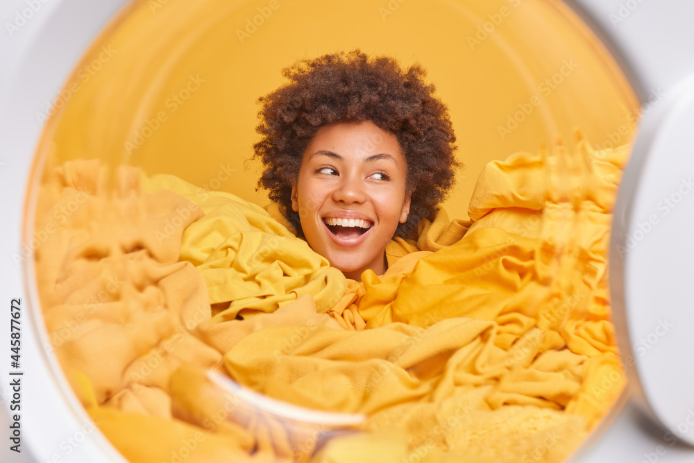 Cheerful Afro American woman with curly hair looks away happily drowned ...