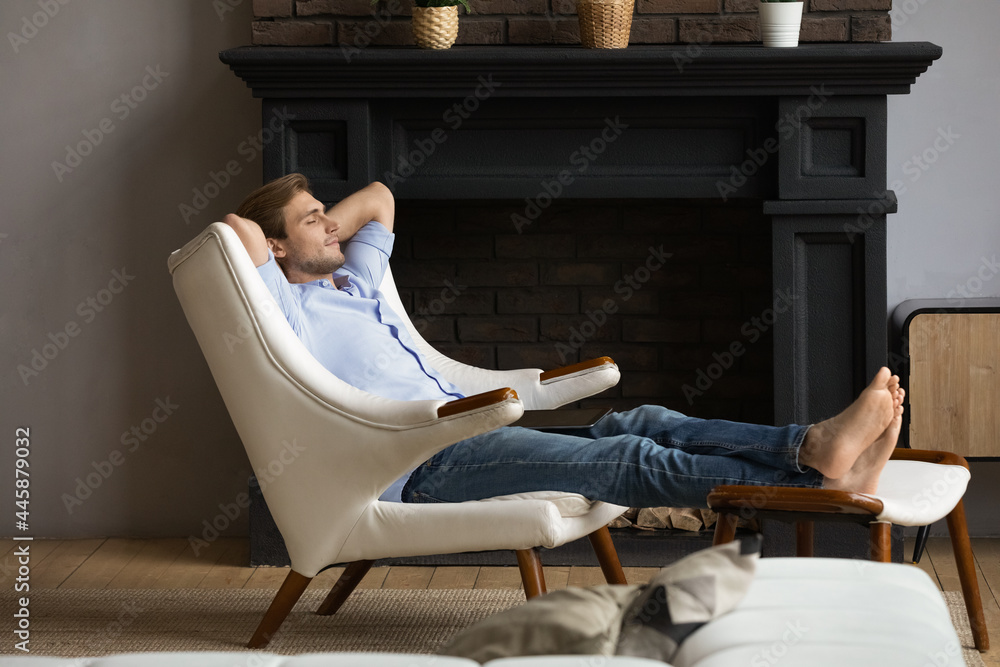Carefree young male homeowner relaxing barefoot in capacious armchair ...