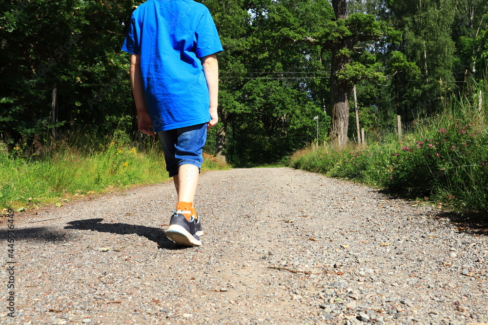 Headless kid walking at a graveled road. Blue shirt and jeans shorts ...