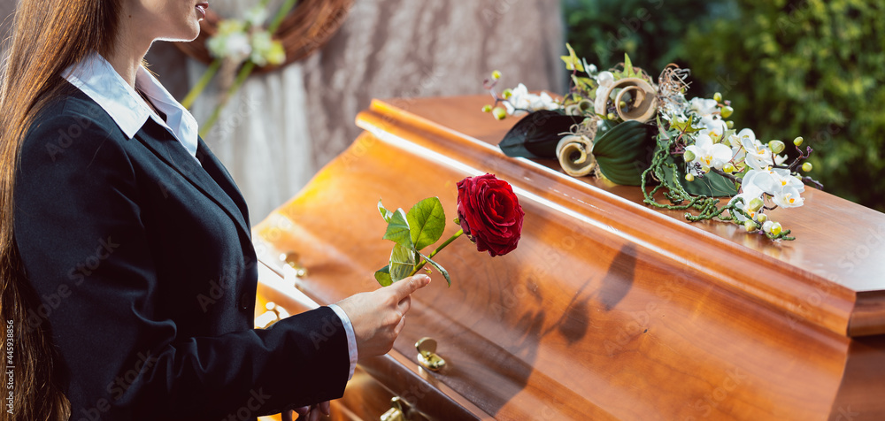 Mourning woman on funeral with red rose standing at casket or coffin ...
