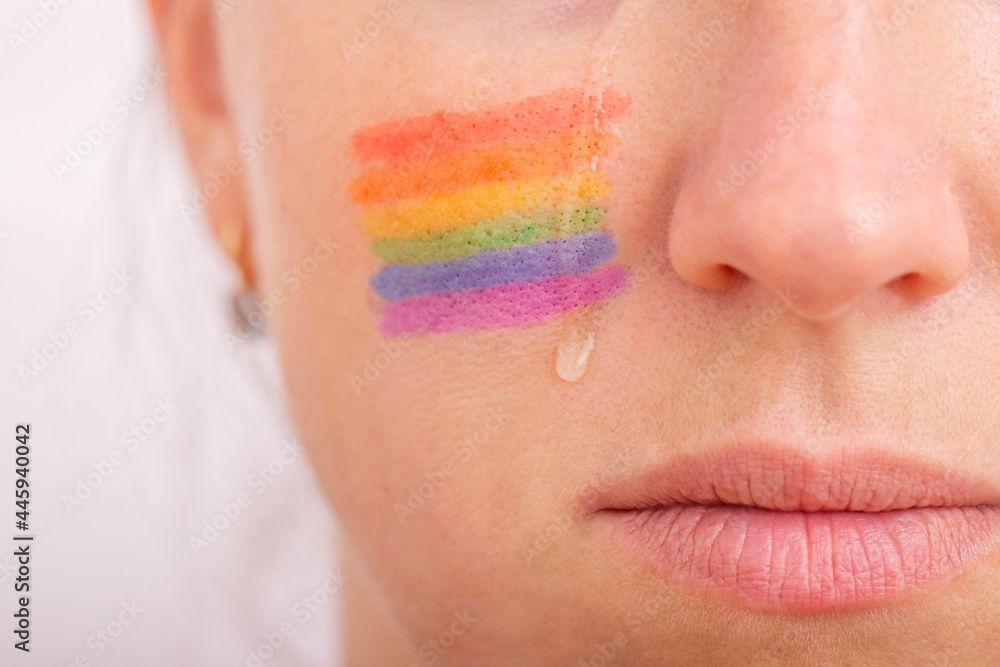 Part of the face of a young crying woman with a painted LGBT flag on ...