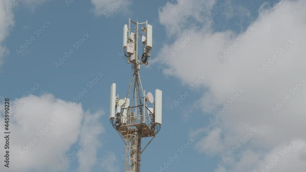 Cell tower on background of blue sky with running clouds in city, time lapse. Cellular base ...