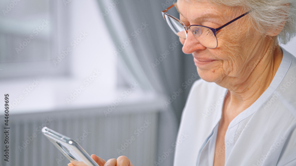 Grey haired old grandmother in glasses looks downward and smiles ...