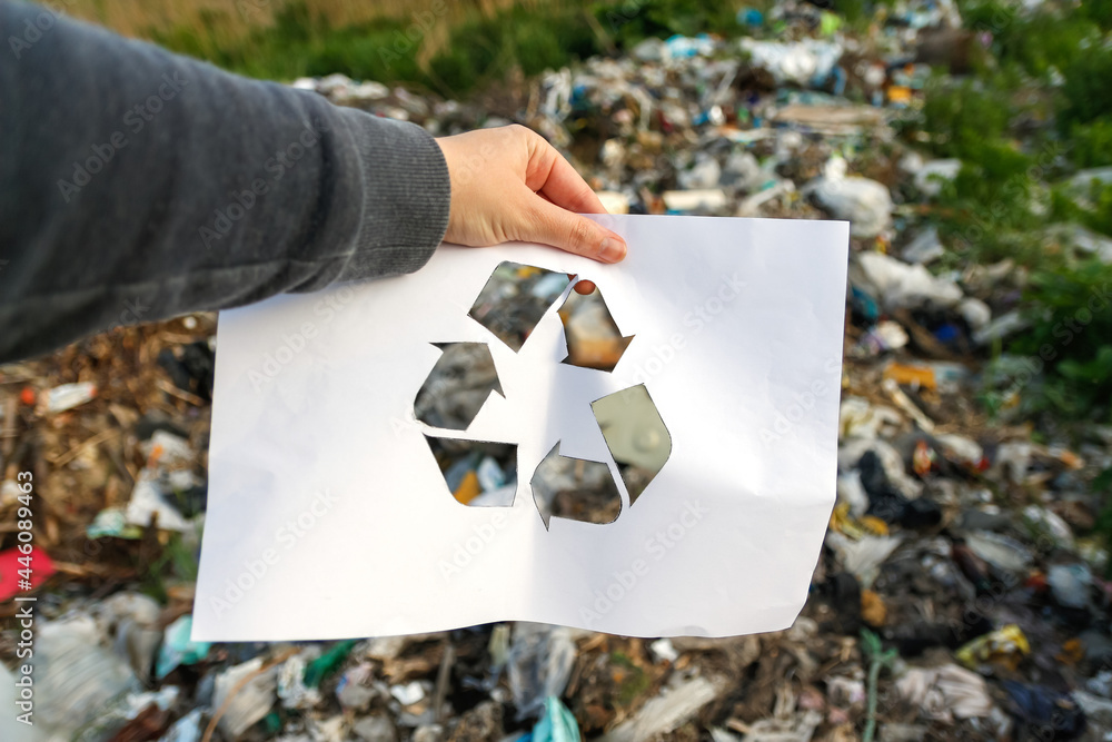 Hand holding cut paper with the logo of recycling on dump garbage trash ...