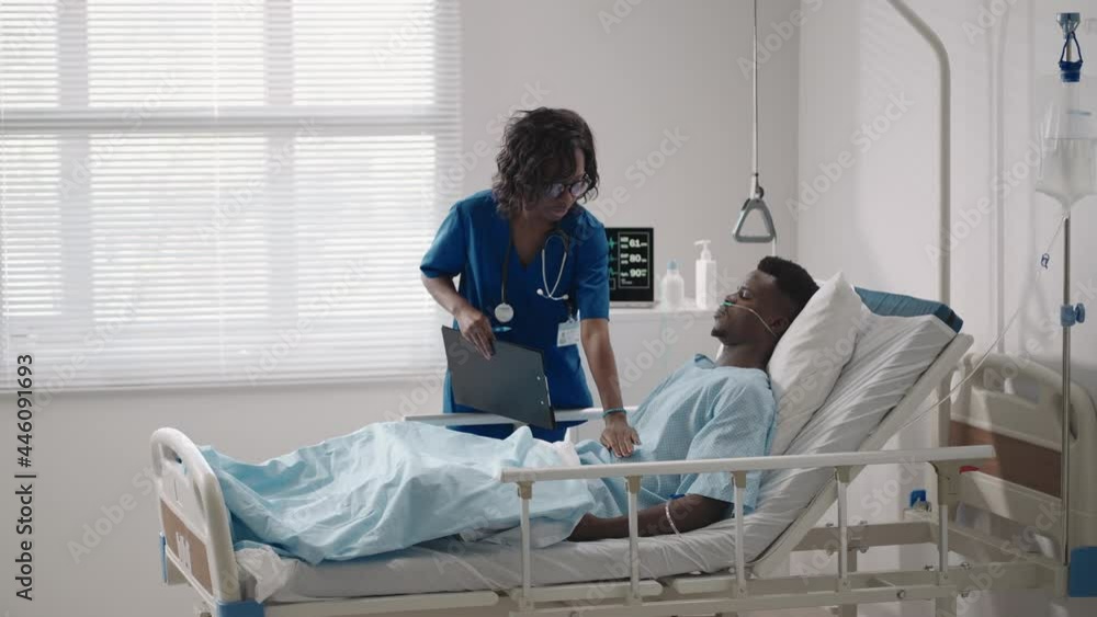 A black female doctor is talking to a black male patient lying on a ...