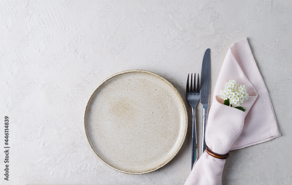 Beige ceramic plate, cutlery and napkin on a beige stone table. Knife ...