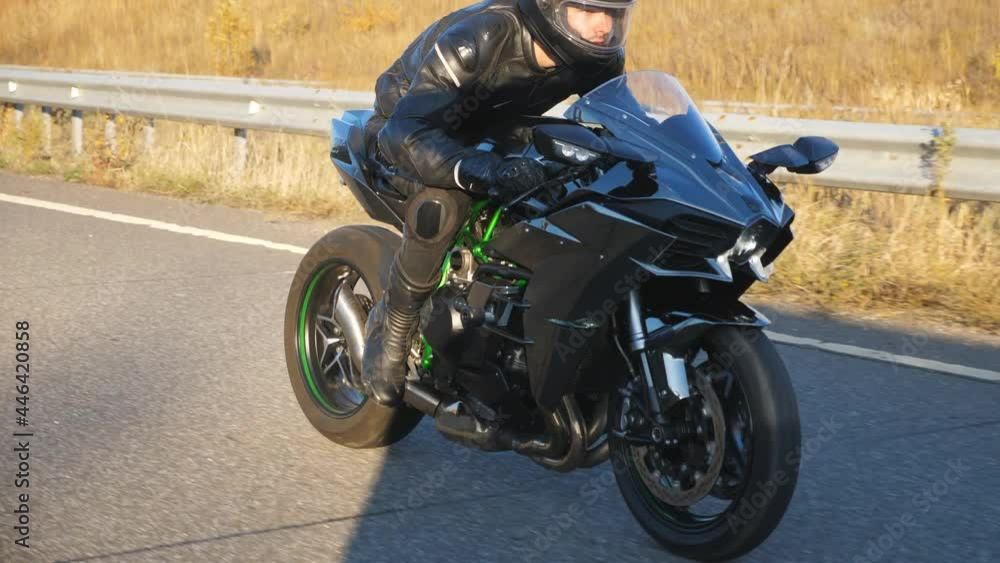 Side view of man in helmet riding on a motorbike at highway in autumn ...