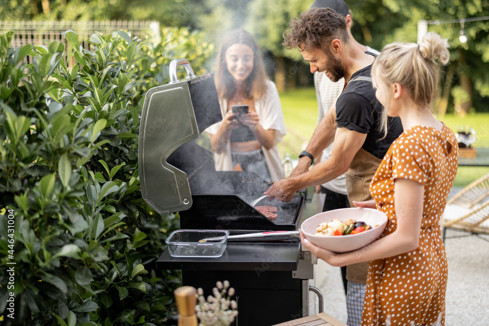 Happy young friends hanging out together, grilling vegetables and meat ...