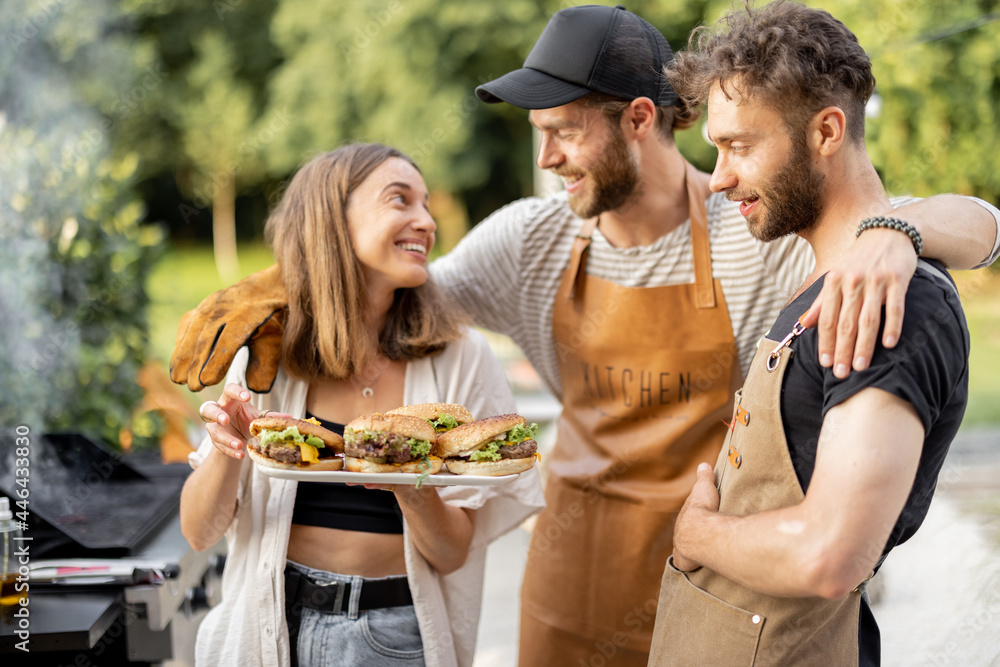 Young people enjoy yummy burgers made on a grill at picnic, standing ...