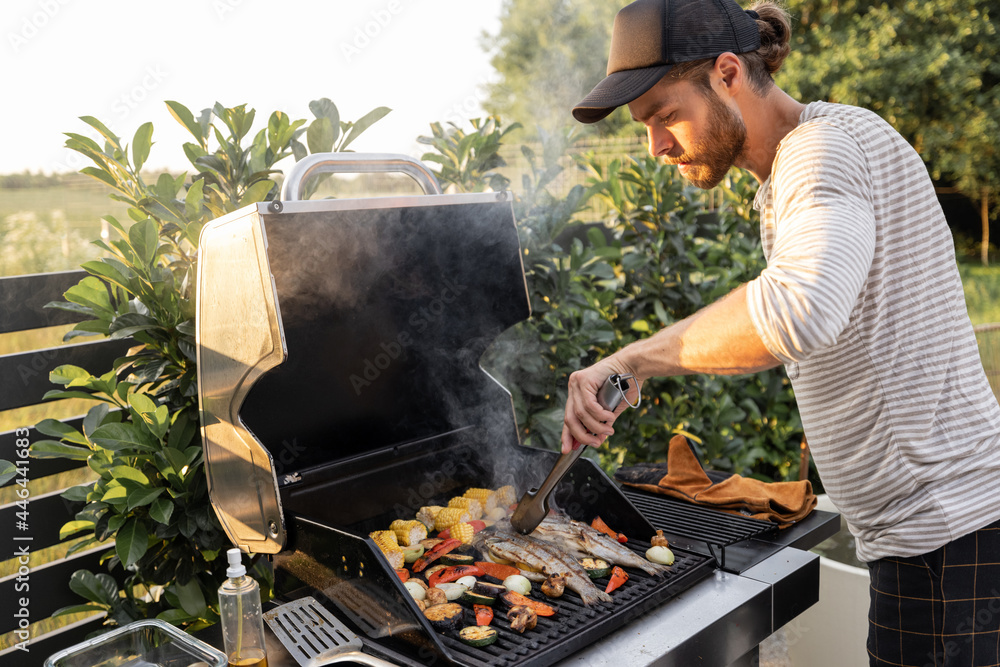 Man cooking vegetables and fish on the modern gas grill at backyard on ...