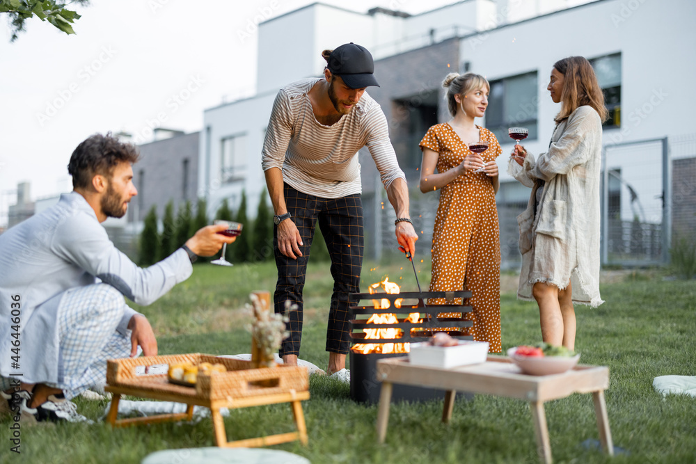 Friends have a picnic, making fire at barbeque and talking on the green ...