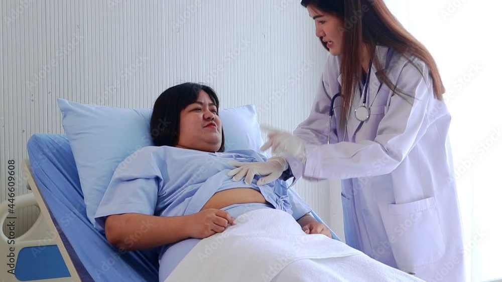 Asian female doctor talking to obese female patient lying in hospital ...